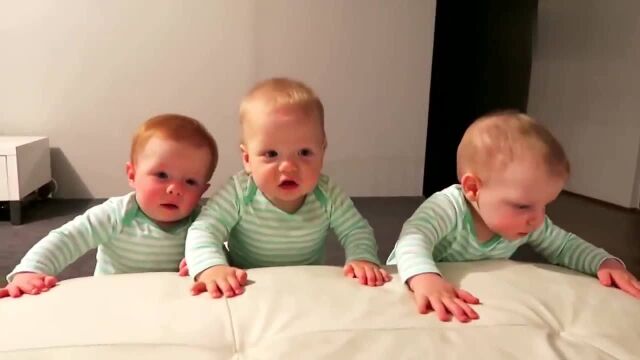 The triplets are standing on the sofa, and the baby in the middle is ...